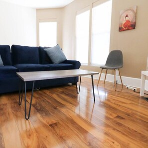 Uma sala de estar moderna com um sofá azul escuro, uma poltrona cinza e uma mesa de centro de madeira.
