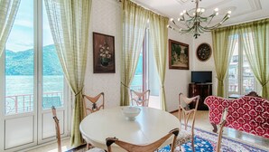 Quarto com uma grande janela, mesa de jantar, cadeiras, sofá e lustre.