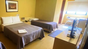 Quarto de hotel com duas camas, uma escrivaninha com computador e uma janela com persianas.