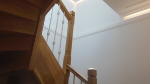 Uma escada de madeira com uma janela de vidro no topo, que leva a um teto branco com iluminação embutida.