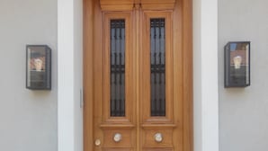 Uma porta dupla de madeira com design tradicional, acompanhada por duas luminárias fixadas na parede.