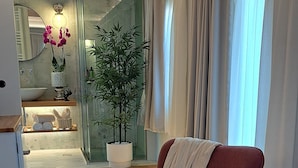 Uma sala de estar moderna com uma poltrona vermelha, uma pequena mesa com um vaso de flores e uma garrafa de vinho.