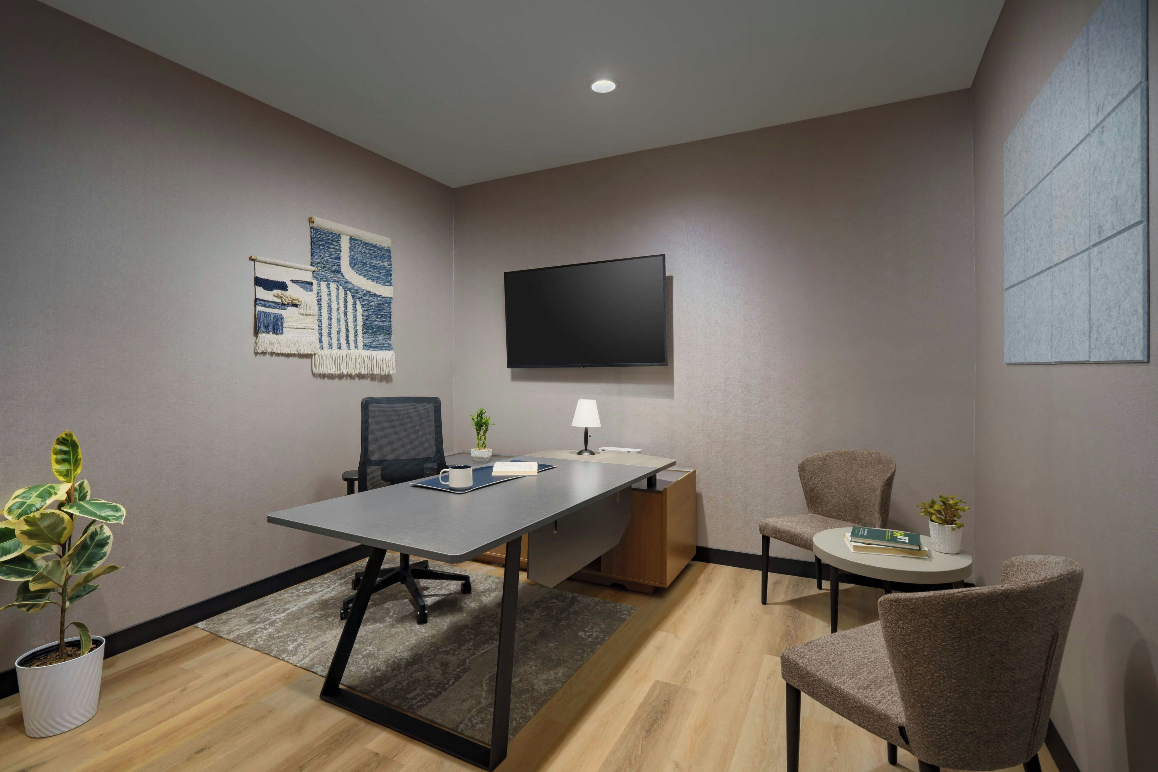 Uma sala de conferências com uma mesa, cadeiras, uma TV e uma planta.