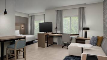 Quarto de hotel moderno com cama, escrivaninha, cadeira, TV e sofá.