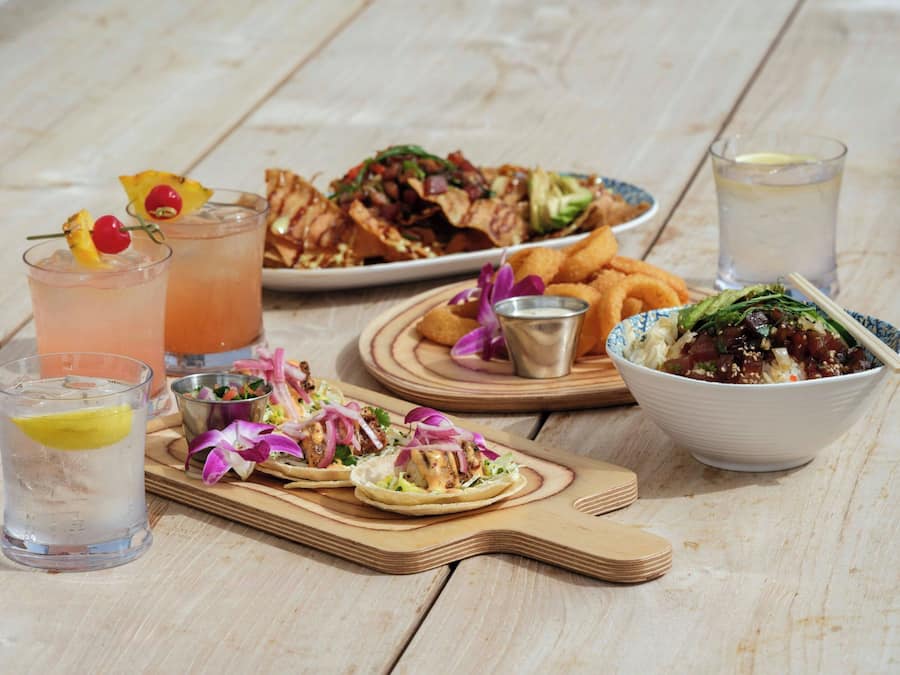 Uma mesa de madeira com diversos pratos, incluindo tacos, uma salada e bebidas.