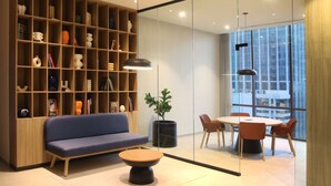 Um interior moderno com um sofá modular, uma mesa de centro redonda, uma estante de livros e uma área de jantar com cadeiras e uma mesa.