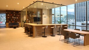 Uma área de bar moderna com divisória de vidro, banquetas e um espaço de estar com mesa e cadeiras.