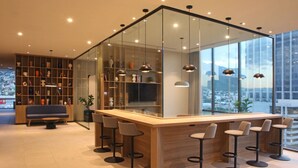 Uma área de bar moderna com balcão de madeira, banquetas e divisória de vidro.