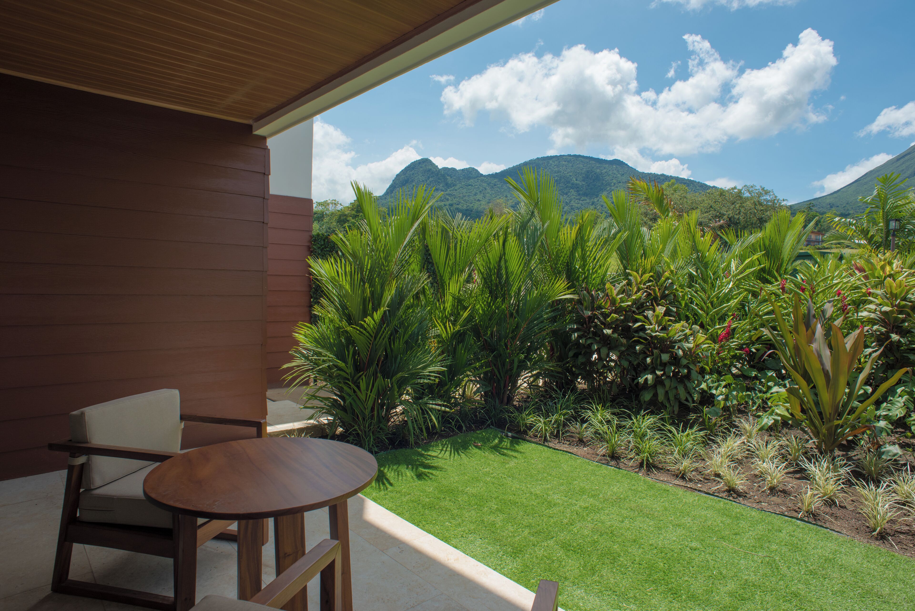 Um pátio com uma mesa e cadeira de madeira, rodeado por vegetação exuberante e vista para montanhas.