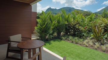 Um pátio com uma mesa e cadeira de madeira, rodeado por vegetação exuberante e vista para montanhas.