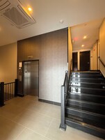Um saguão de hotel com escadas, elevador e parede com textura.