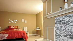 Quarto com cama, uma cadeira, mesinha e lareira de mármore.