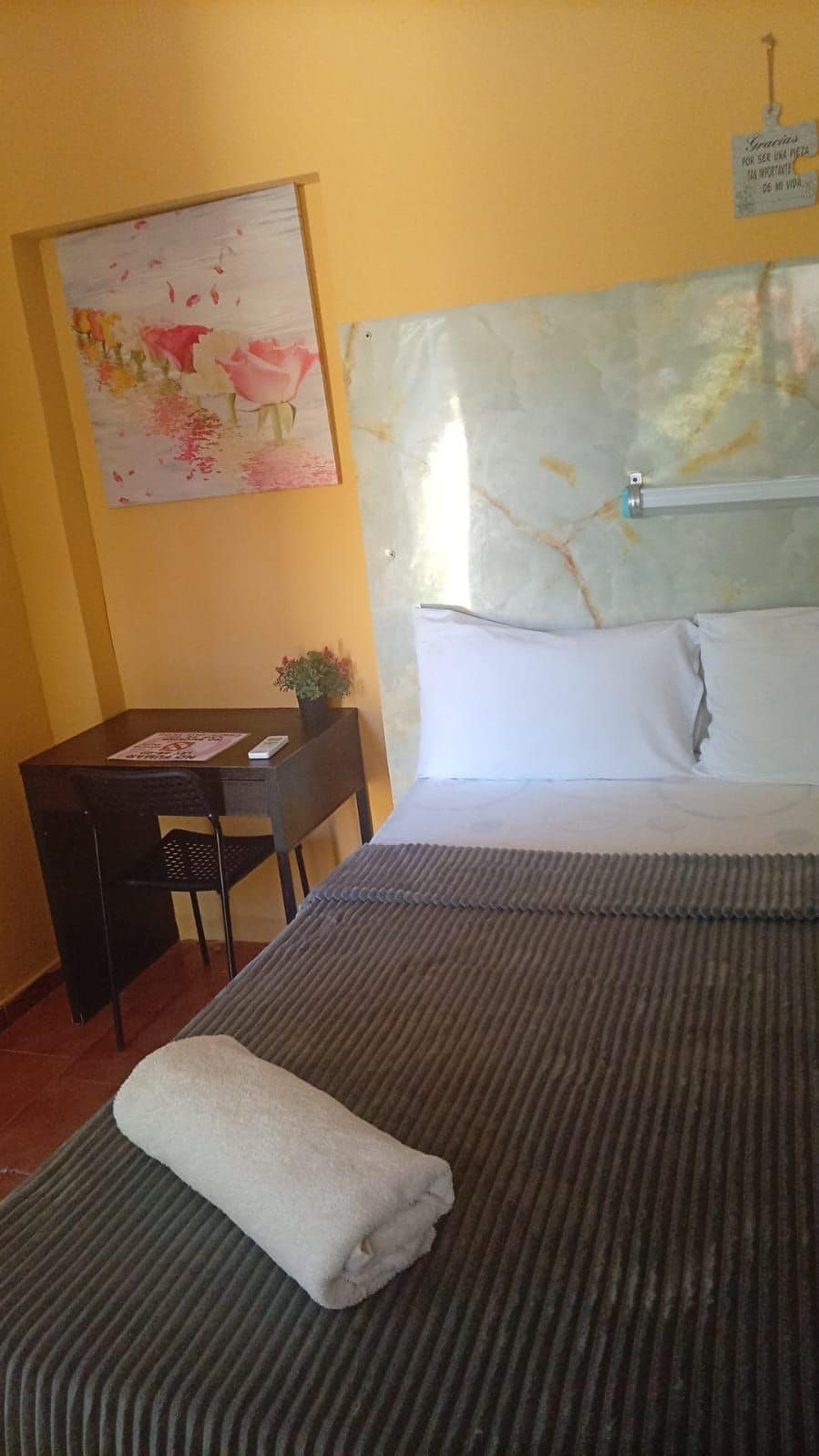 Quarto de hotel com uma cama, uma escrivaninha e uma cadeira.