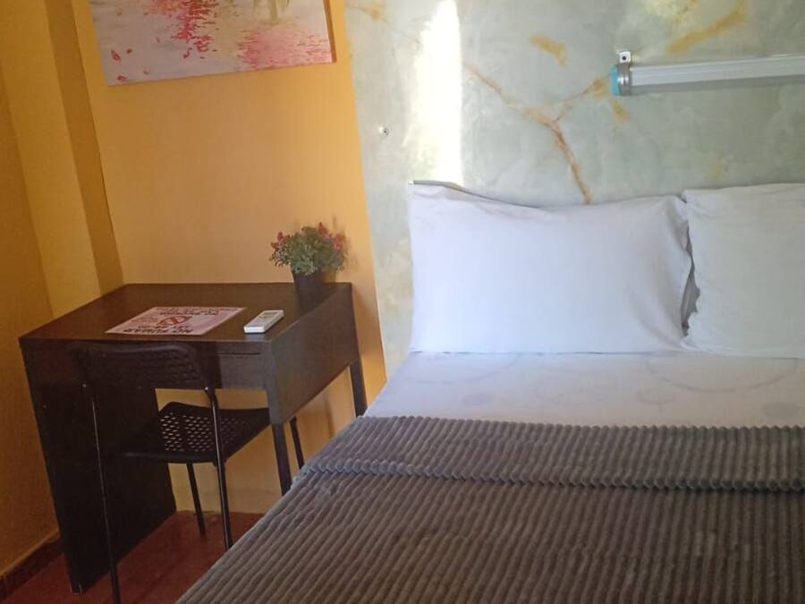 Quarto de hotel com uma cama, uma escrivaninha e uma cadeira.