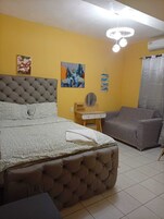 Um quarto com uma cama grande, um sofá cinza, uma mesinha e um espelho.