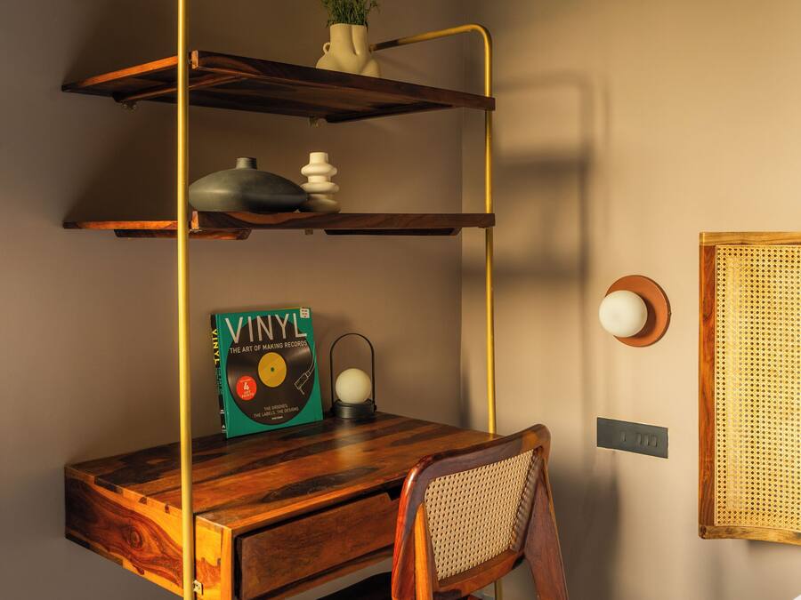 Quarto compacto com escrivaninha de madeira, uma cadeira, estante e luminária fixada na parede.