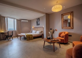 Quarto de hotel com uma cama, uma escrivaninha, uma cadeira, uma mesa de centro redonda e um espelho grande.