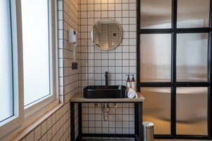 Casa de banho com lavatório preto, espelho, toalha e um cesto de lixo.