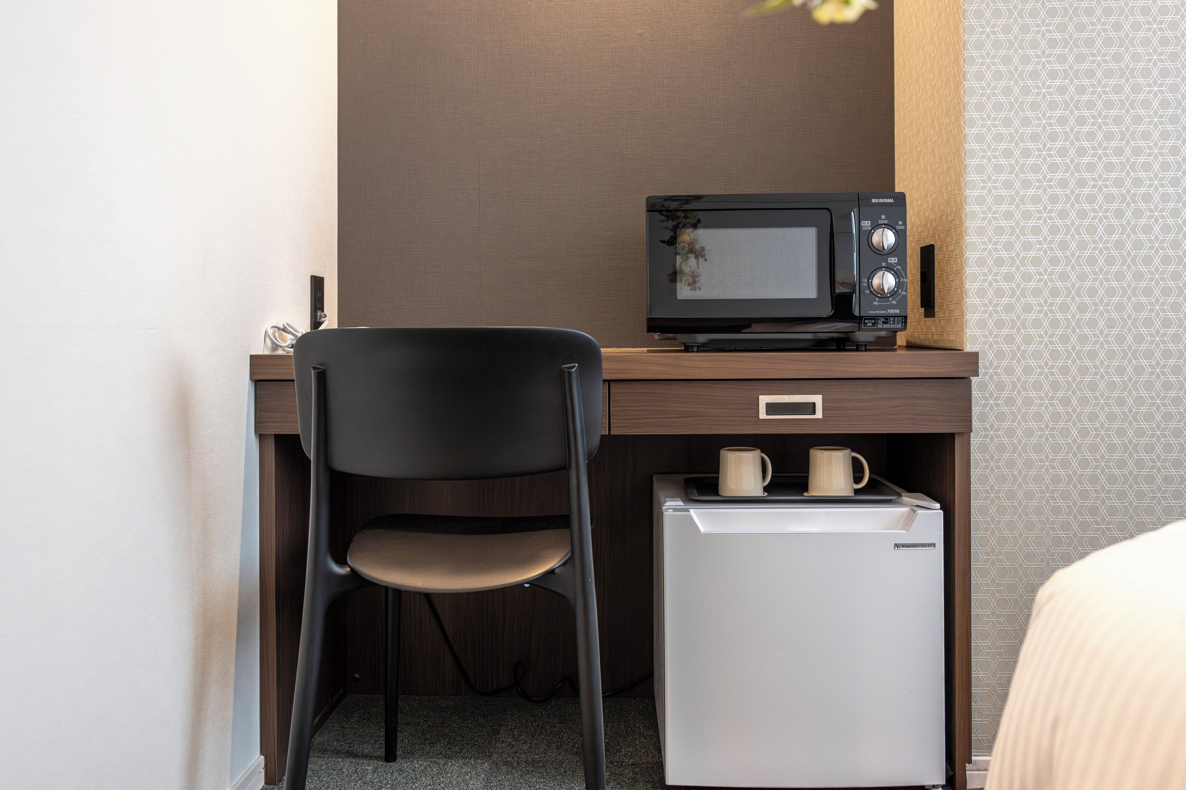Uma cozinha compacta equipada com micro-ondas, mini-geladeira e uma cadeira.