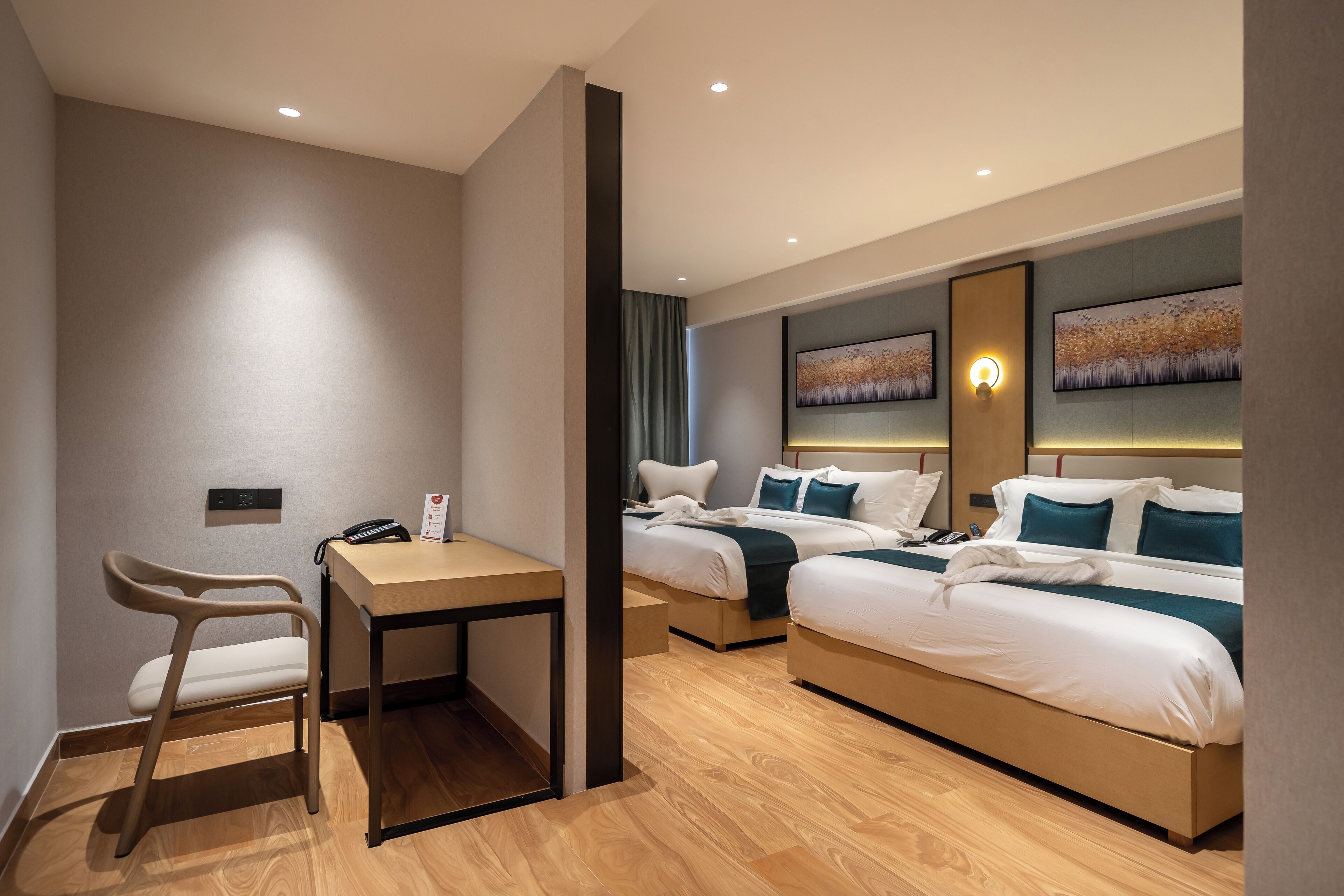 Quarto de hotel com duas camas, uma escrivaninha, uma cadeira e obras de arte nas paredes.