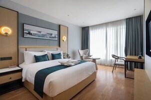 Quarto de hotel moderno com uma cama grande, uma escrivaninha, uma cadeira e uma televisão.