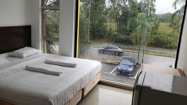 Quarto com cama, almofadas e vista para a estrada com carros.