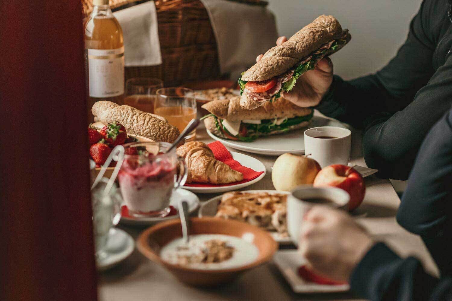 Mesa de café da manhã com sanduíche, croissants e uma tigela de iogurte.