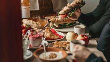 Mesa de café da manhã com sanduíche, croissants e uma tigela de iogurte.