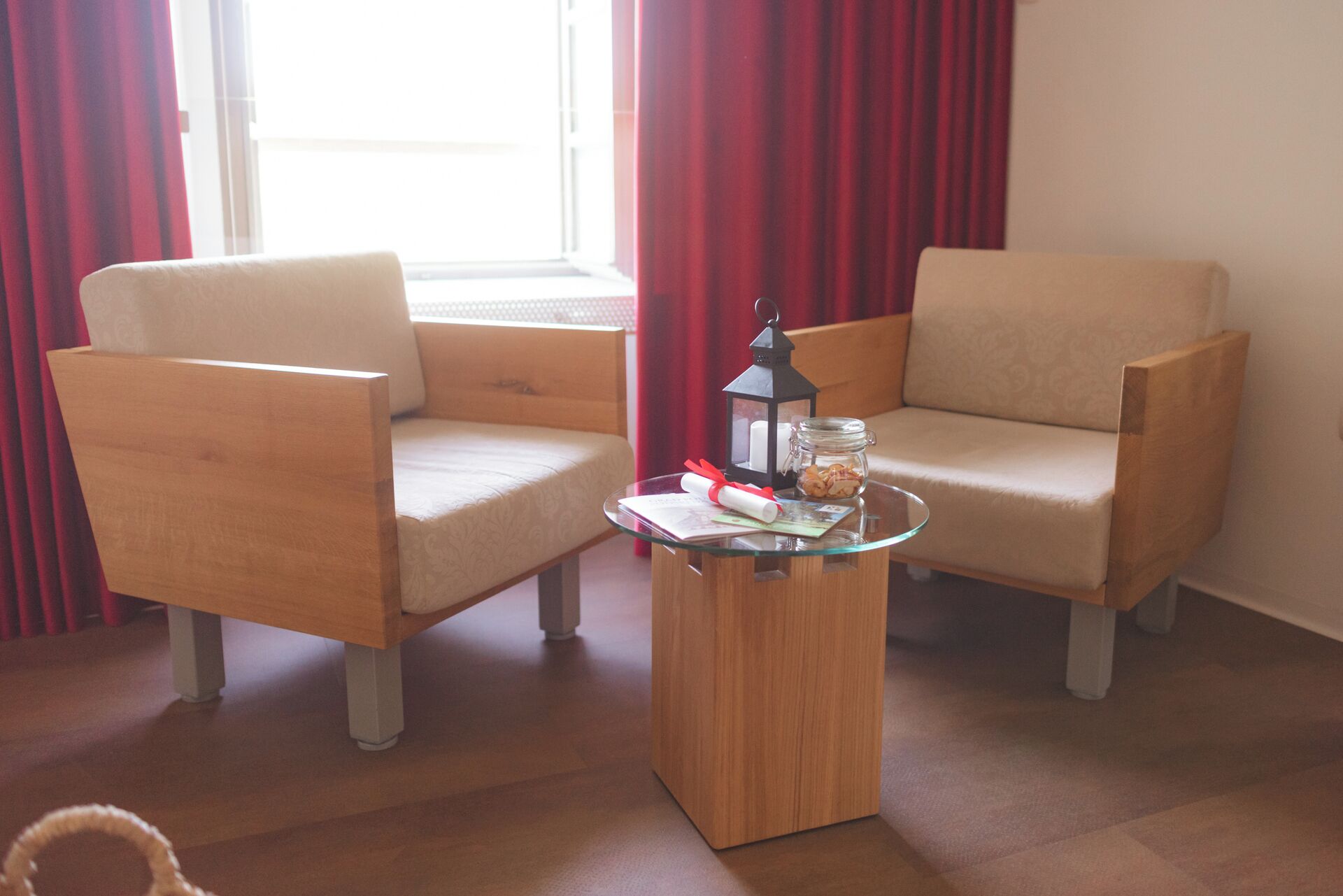 Duas poltronas bege de frente uma para a outra, com uma mesa de centro de vidro no meio. Um candeeiro negro e um frasco com biscoitos estão sobre a mesa.