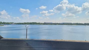 Um lago tranquilo com barcos, céu claro e edifícios ao longe.