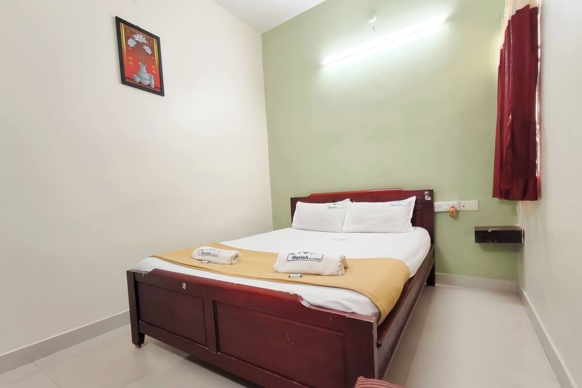 Cama bem arrumada com cabeceira de madeira, mesinha de cabeceira e tomada na parede.