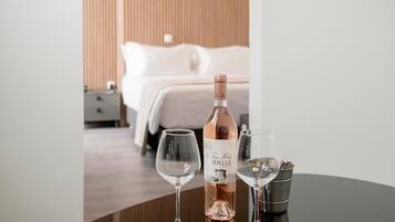 Quarto de hotel com cama, mesa de cabeceira, uma garrafa de vinho e dois copos.