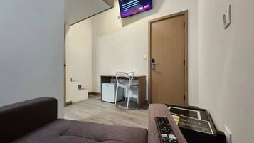 Quarto de hotel moderno com sofá, TV fixada na parede, escrivaninha com cadeira e uma porta.