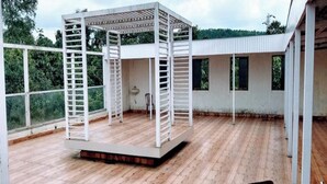 Uma área externa coberta com piso de madeira, estrutura de metal branco e uma cadeira.