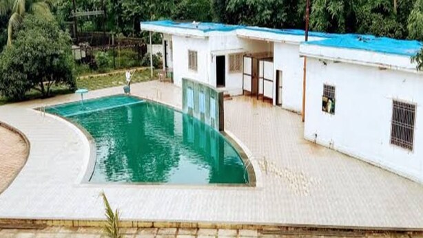 Uma piscina com borda curva, uma área externa coberta e um edifício com telhado azul.