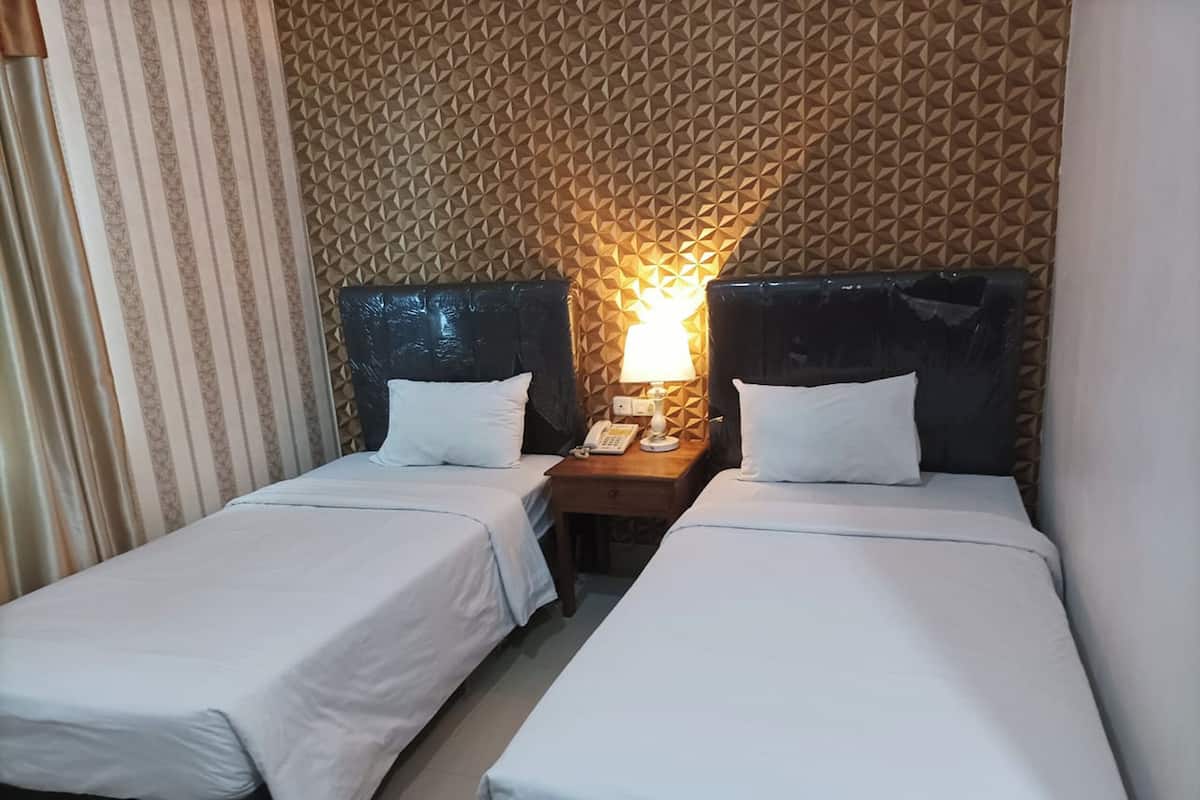 Quarto de hotel com duas camas de solteiro, mesa de cabeceira com abajur e parede com padrão geométrico.