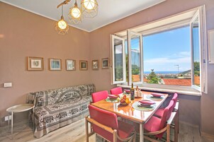 Uma sala de jantar com uma mesa posta para quatro pessoas, um sofá e uma janela com vista.