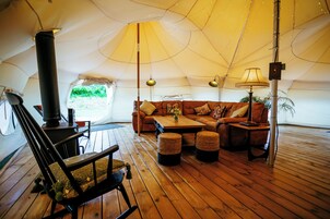Interior de uma tenda com sofá, pufes, cadeira de balanço e mesa.
