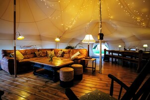 Acomodação em tenda com piso de madeira, sofás de couro e mesas.
