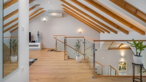 Um loft espaçoso com pé direito alto, vigas de madeira, escada de vidro e plantas em vasos.