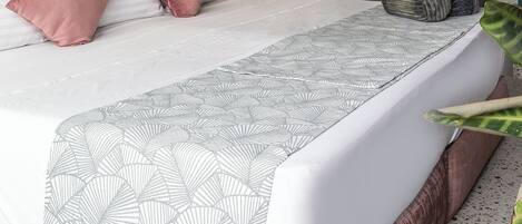 Quarto moderno com cama grande, almofadas rosa e brancas, colcha estampada e luminária pendente.