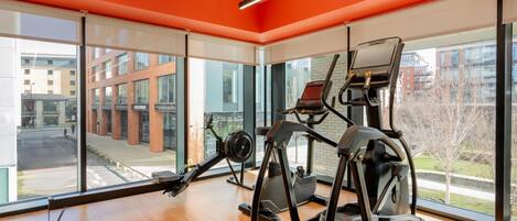 Ginásio com equipamentos de cardio e amplas janelas com vista para a cidade.