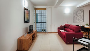 Um espaço de estar compacto com um sofá vermelho, um móvel de TV de madeira e uma porta de vidro que dá para uma varanda.