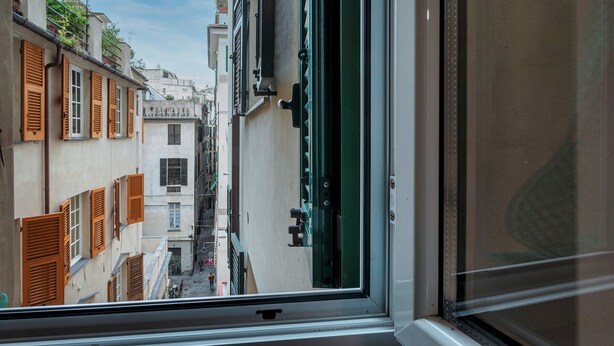Vista de uma rua estreita pela janela, com edifícios com portadas de madeira e uma porta verde.