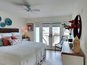 Quarto com cama, mesa de cabeceira, cadeira, escrivaninha, espelho e vista para o exterior.