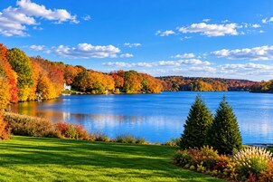 Um lago rodeado por folhagem outonal, um primeiro plano com grama e um céu claro.