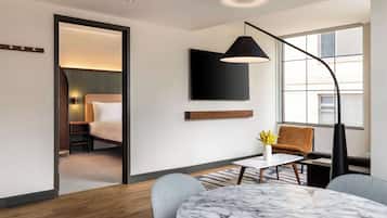 Quarto de hotel moderno com cama, mesa de jantar, sofá e uma janela grande.
