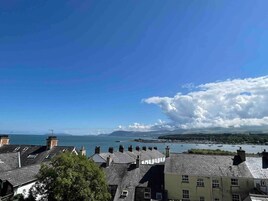 Uma cidade costeira com casas em socalcos, céu azul límpido e vista para o mar e colinas distantes.