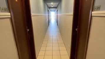 Um corredor comprido e estreito, com chão de azulejos e portas de madeira em ambos os lados.