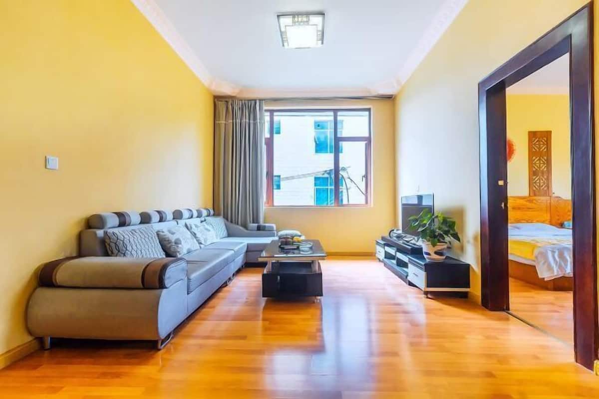 Uma sala moderna com sofá, mesa de centro e uma cama no quarto adjacente.